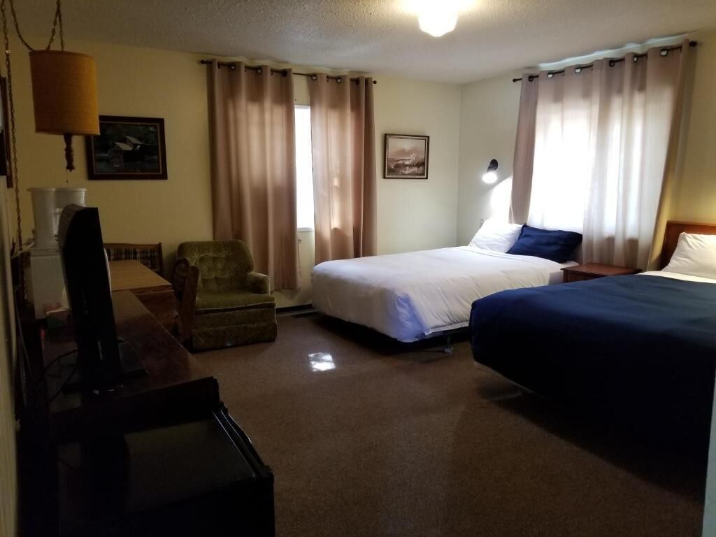 Quarto de hotel com cama, cadeira, escrivaninha e cortinas.