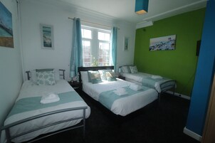 Quarto de hotel com duas camas de solteiro, janela com cortinas e uma parede de destaque verde.