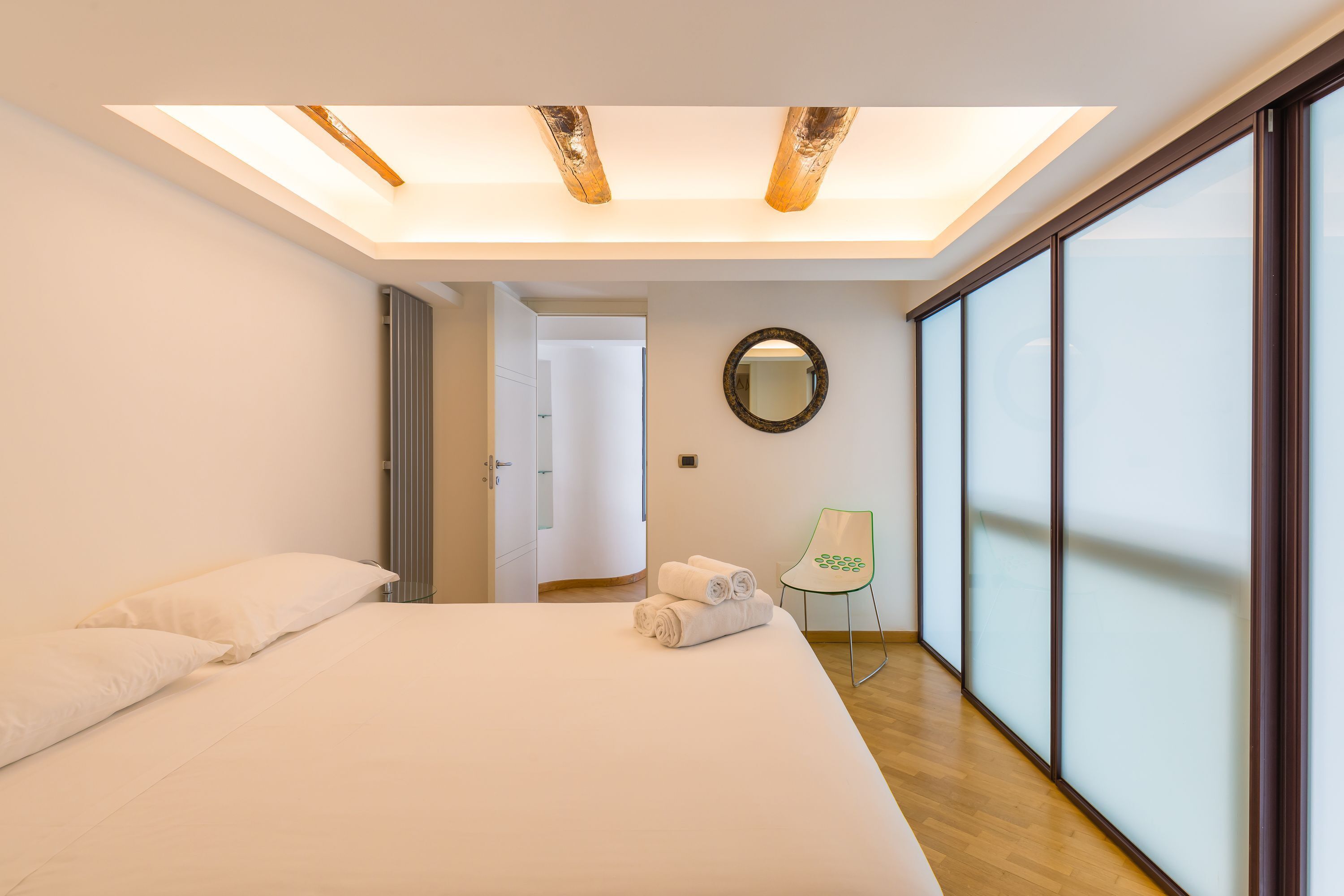 Quarto de hotel moderno com uma cama grande, claraboia, espelho e vista através de janelas do chão ao teto.