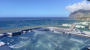 Uma área de hidromassagem com vista para o oceano e uma costa montanhosa.