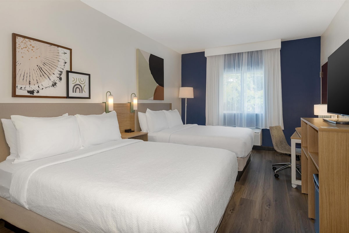 Quarto de hotel com duas camas, uma escrivaninha, uma cadeira e uma televisão.