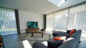 Uma sala de estar moderna com um sofá cinza, uma mesa de centro de madeira e uma televisão de tela plana sobre um suporte de madeira.