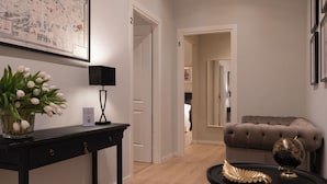 Um corredor com uma mesa consola preta, um vaso de tulipas brancas, um mapa emoldurado, um candeeiro preto e uma mesa redonda com um globo e objeto decorativo.