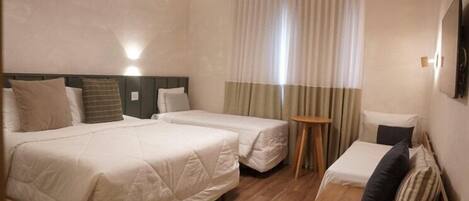 Quarto de hotel com duas camas, uma mesinha e uma televisão fixada na parede.
