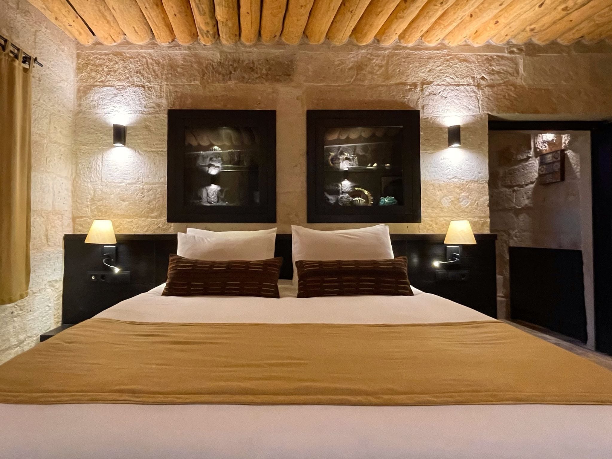 Quarto com uma cama grande, duas mesas de cabeceira e luminárias fixadas na parede.