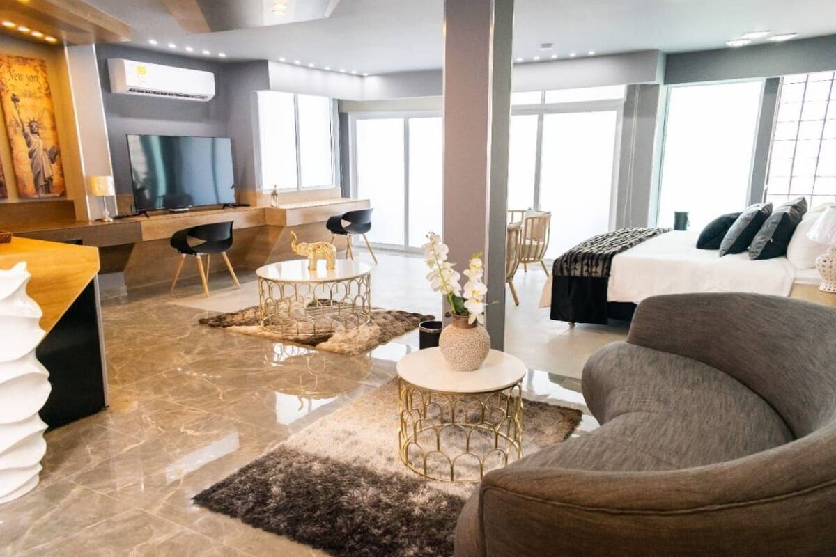 Quarto de hotel moderno com cama, sofá, escrivaninha e televisão.