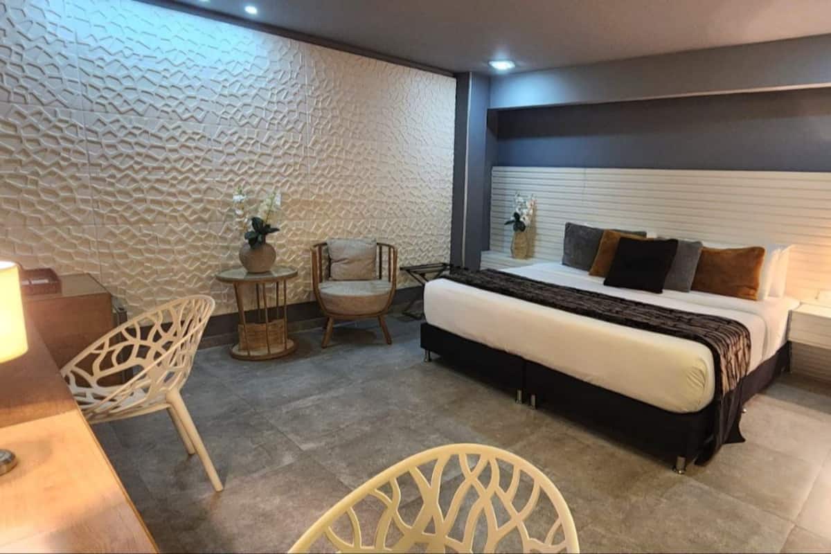 Quarto moderno com uma cama grande, duas cadeiras, uma mesinha e uma luminária.