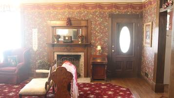 Quarto tradicional com lareira, um banco de madeira, um tapete floral vermelho e uma porta com um espelho grande acima.