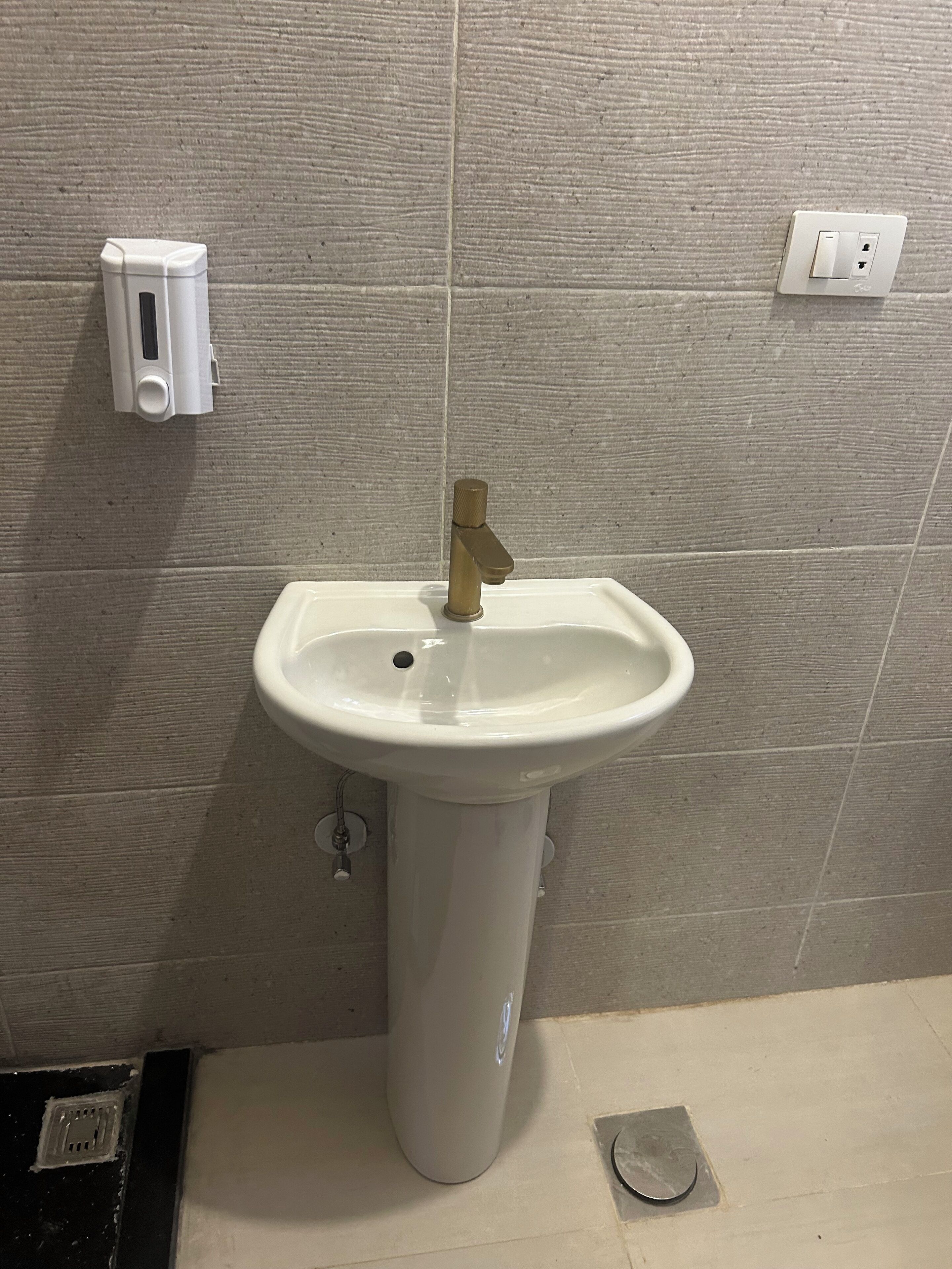 Uma pia de banheiro com uma torneira simples, um dispensador de sabonete e uma tomada na parede.