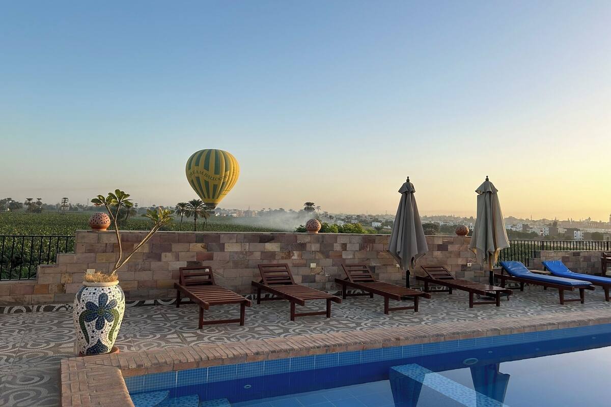 Área de piscina no terraço com espreguiçadeiras, um balão de ar quente ao fundo e vista para a cidade.