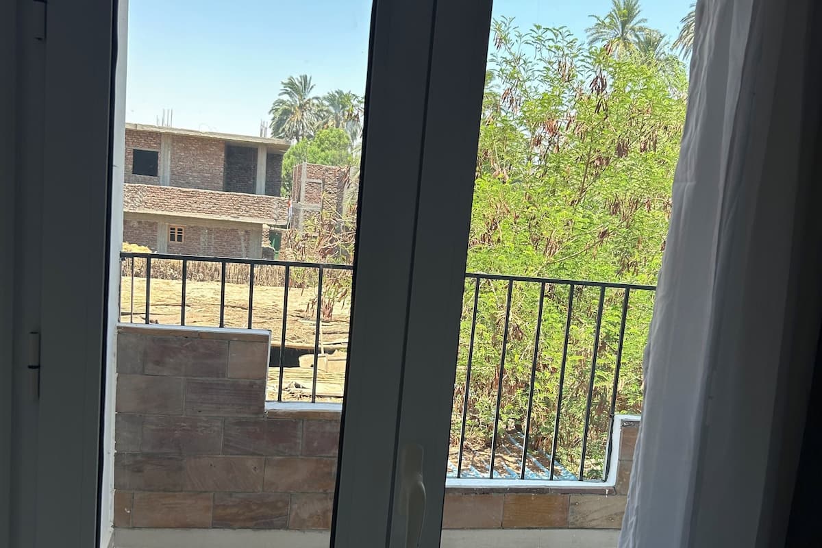 Vista de uma varanda com guarda-corpo de metal, parede de pedra e um edifício ao fundo.