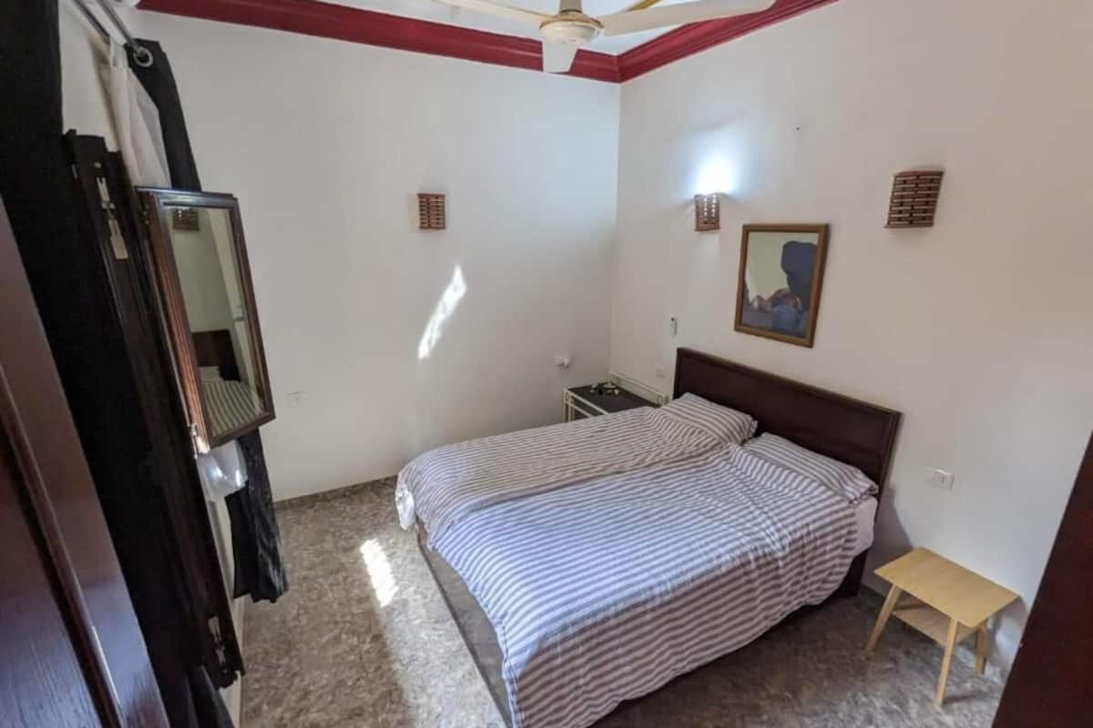 Quarto com duas camas, um ventilador de teto, uma mesa pequena e um espelho.