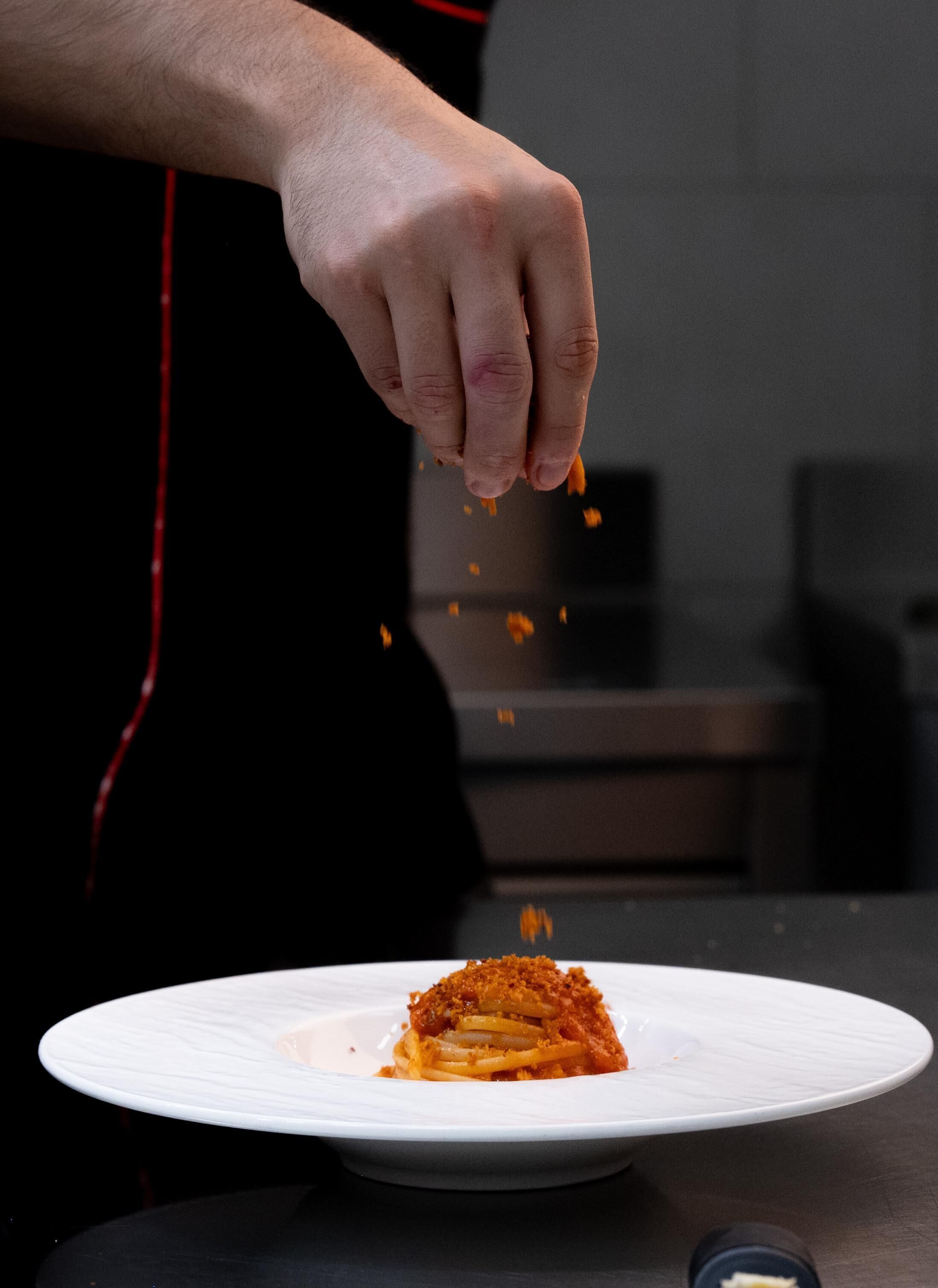 Uma mão polvilhando tempero sobre um prato com comida.