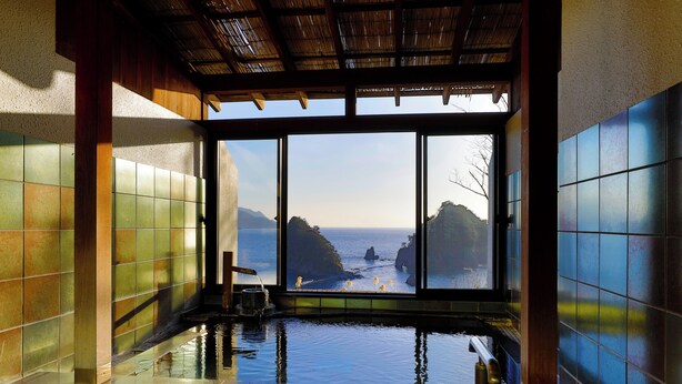 Quarto com uma grande janela com vista para a água e falésias.