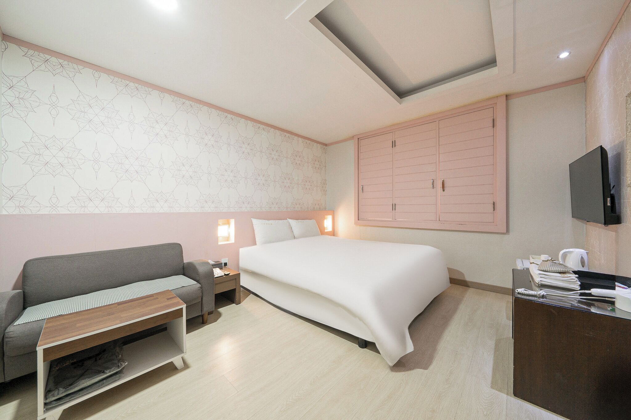 Quarto de hotel com cama, sofá, escrivaninha, guarda-roupa e televisão.