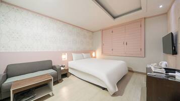 Quarto de hotel com cama, sofá, escrivaninha, guarda-roupa e televisão.