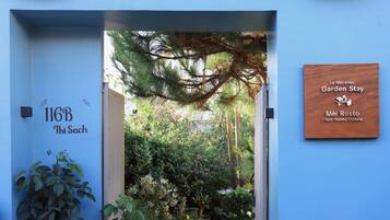 Uma porta azul com uma placa indicando '116B The Sach' e outra placa para 'Le Macaron Garden Stay' com o logotipo de uma culinária à base de plantas.
