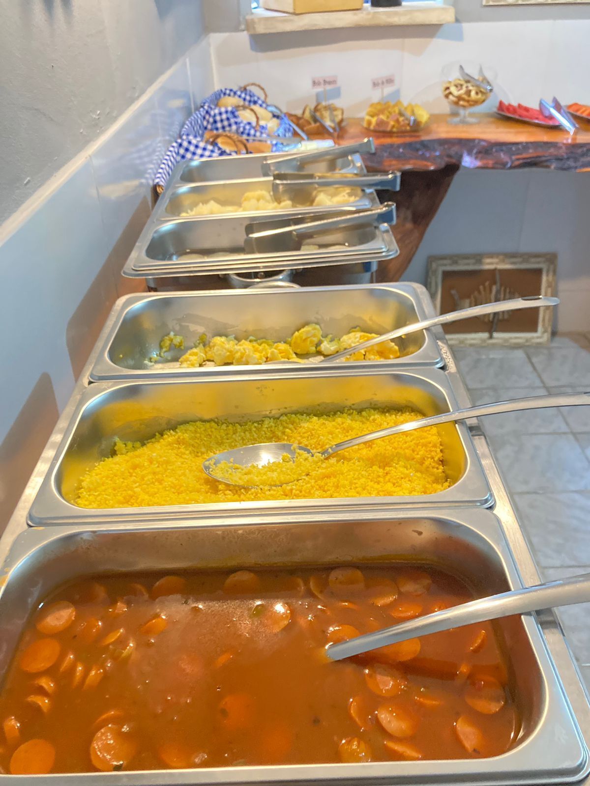 Buffet variado com diversas opções de comida, incluindo ovos mexidos, couscous e um prato à base de tomate.