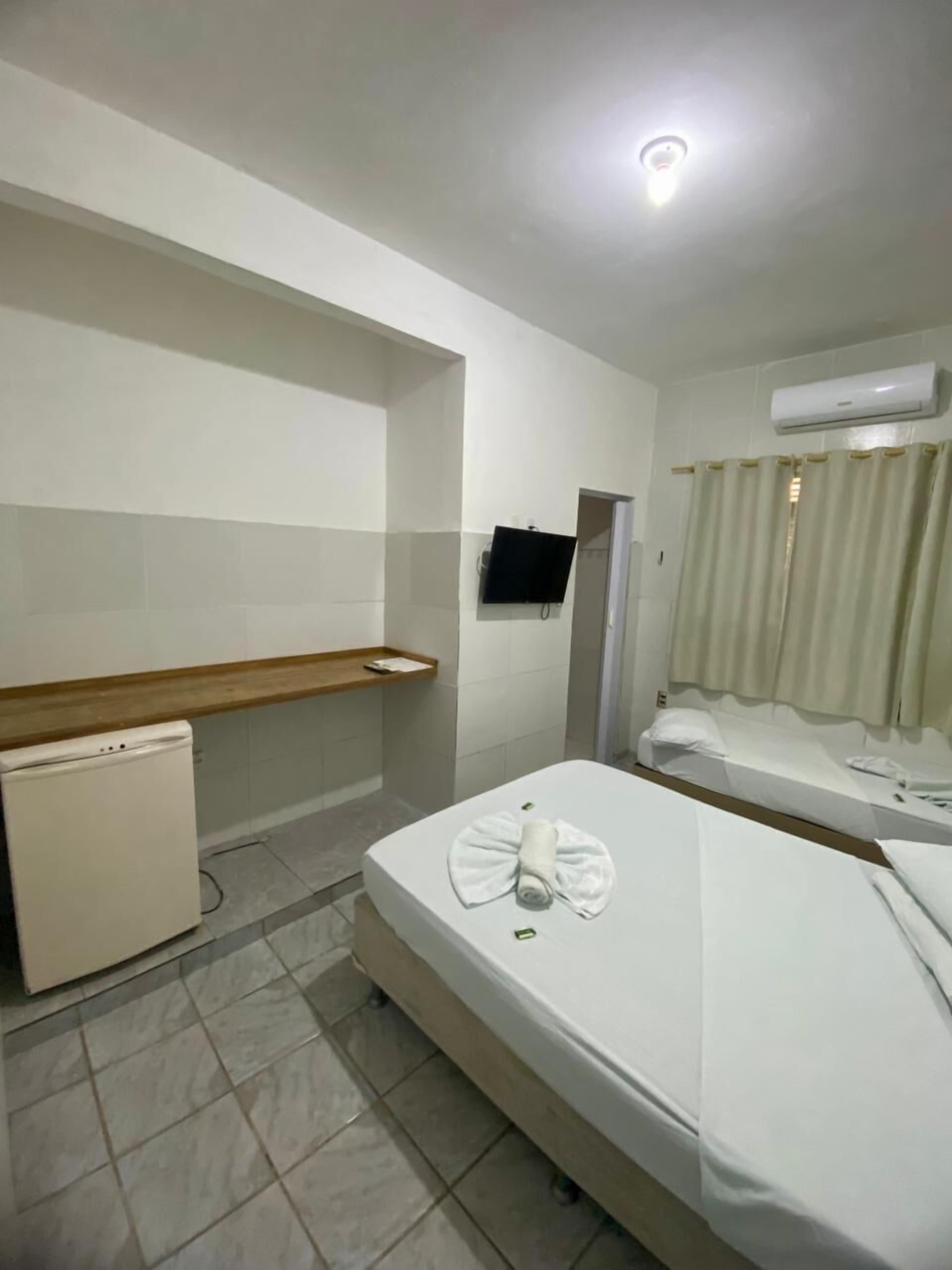 Quarto de hotel com cama, secretária pequena, televisão e unidade de ar condicionado.