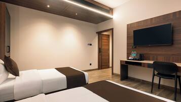 Quarto de hotel com duas camas, uma escrivaninha, uma cadeira, televisão de tela plana e uma parede de destaque em madeira.