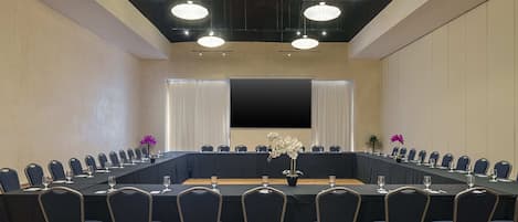 Uma sala de conferências com uma mesa comprida, cadeiras e uma tela de projeção.
