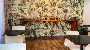 Um restaurante com parede estampada com padrão de folhagem tropical, piso de madeira e assentos modernos.