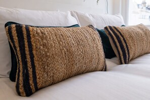 Cama com roupa de cama branca e duas almofadas trançadas com listras escuras.
