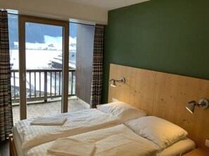 Quarto de hotel com duas camas, uma cabeceira de madeira e vista para uma paisagem nevada através de uma porta de correr.