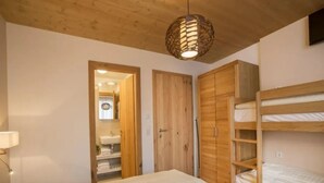 Quarto com duas camas, guarda-roupa de madeira e banheiro visível por uma porta aberta.