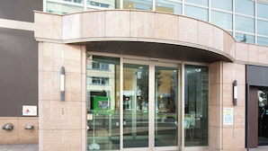 Fachada curva de um edifício, portas de vidro e piso ladrilhado.