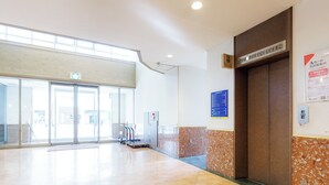 Um hall amplo com entrada de vidro, um painel informativo azul e um elevador de madeira.
