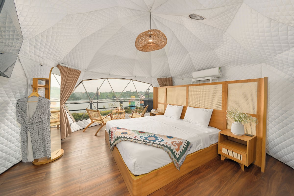 Um alojamento em tenda espaçoso, com uma cama grande, mobiliário de madeira e vista para o exterior.