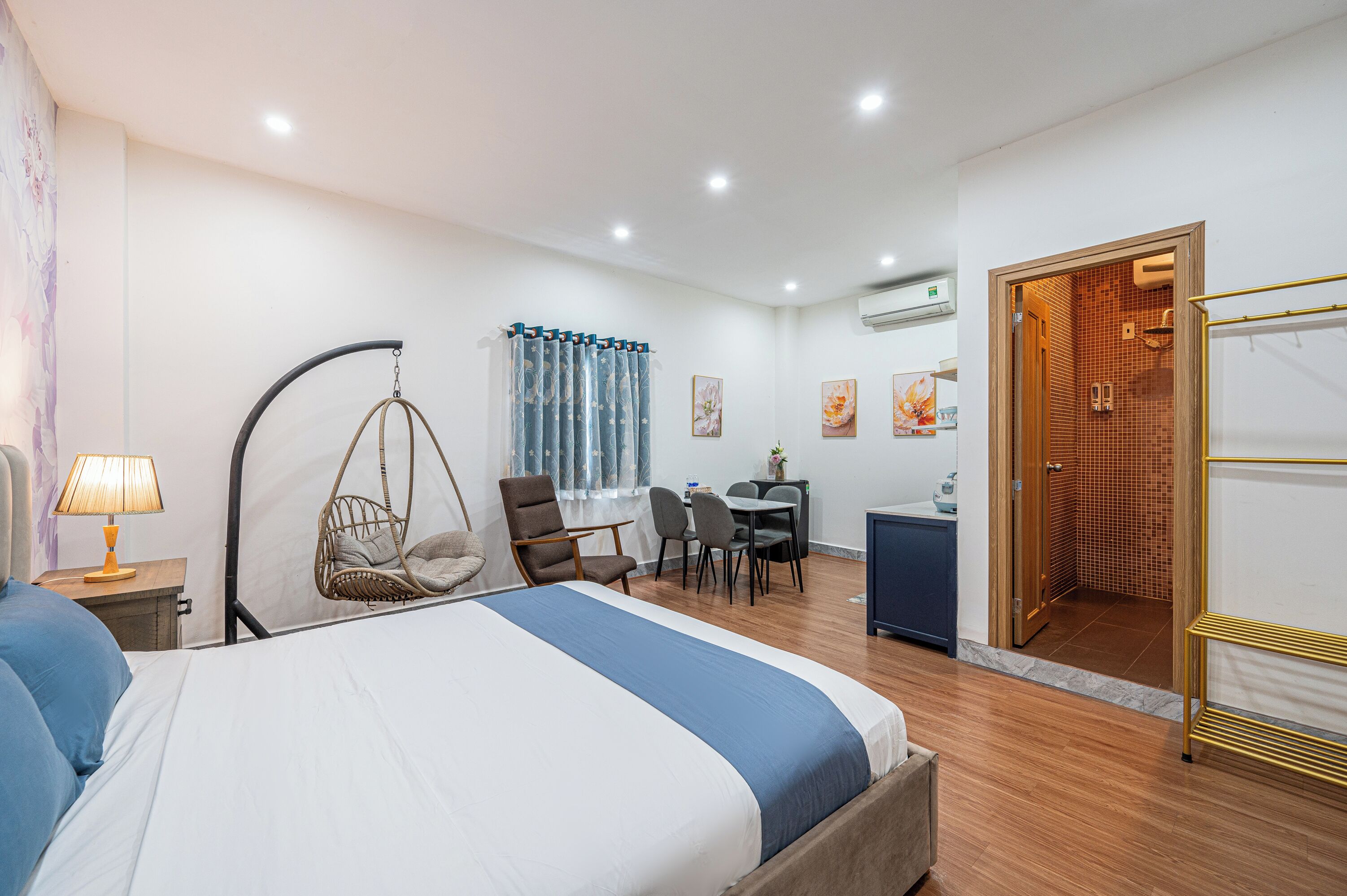 Quarto de hotel com cama, escrivaninha, cadeira, balanço e área de chuveiro.