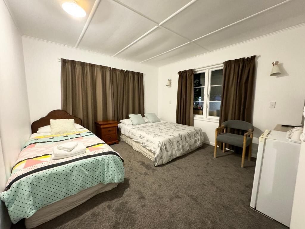 Quarto com duas camas, uma escrivaninha, uma cadeira e uma janela com cortinas.