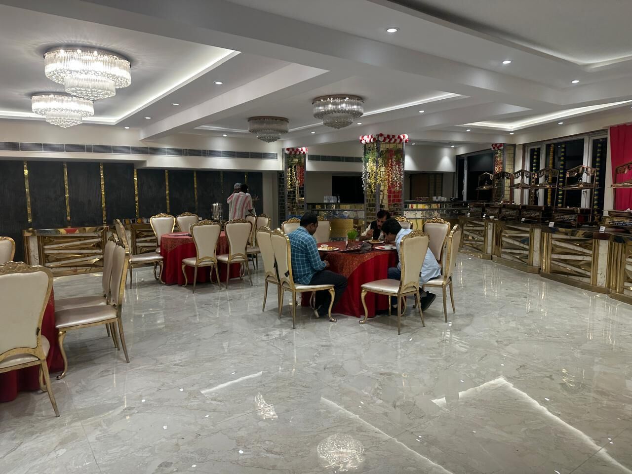 Uma área de jantar ampla com piso de mármore, cadeiras com detalhes dourados e lustres.
