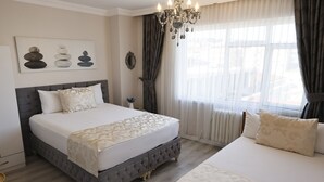Quarto com uma cama grande, uma cama menor, um lustre e uma janela com cortinas.