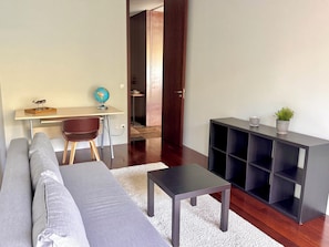 Uma sala de estar com sofá, uma mesinha, uma escrivaninha com globo, estante e porta que dá para outro cômodo.