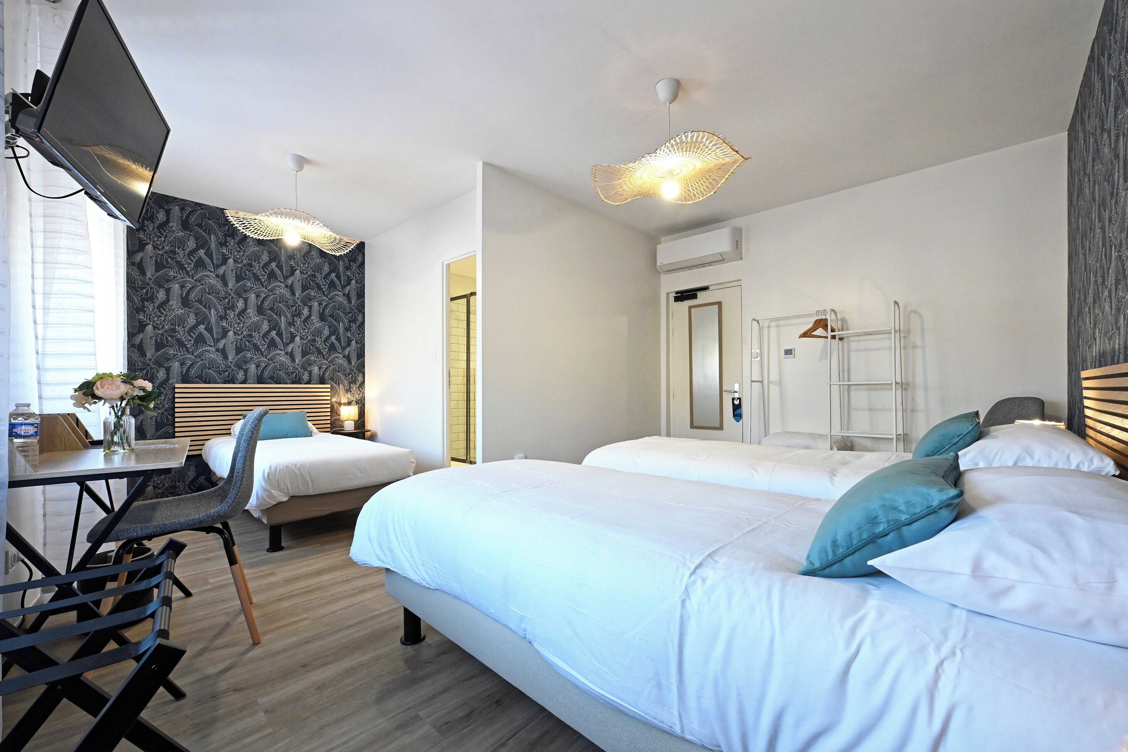Quarto de hotel com duas camas, uma escrivaninha com cadeira, televisão e parede estampada.