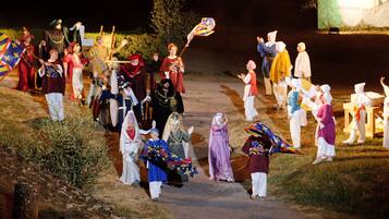 Um grupo de pessoas em trajes históricos reunido em uma área gramada ao ar livre durante a noite.