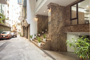 Entrada de hotel com uma escadaria de mármore, plantas em vasos e vista para a rua.