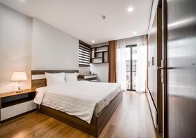 Quarto de hotel moderno com cama de madeira, mesa de cabeceira com luminária, guarda-roupa embutido e vista para o exterior.