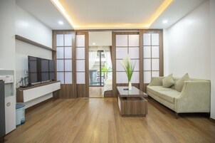 Uma sala de estar moderna com uma televisão de tela plana, um sofá, uma mesa de centro e uma porta deslizante que dá para uma varanda.