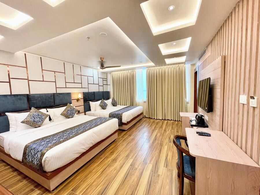 Quarto de hotel com duas camas, uma escrivaninha, uma televisão e iluminação embutida no teto.