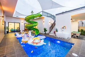 Uma piscina com um escorrega verde, brinquedos infláveis e uma banheira de hidromassagem.