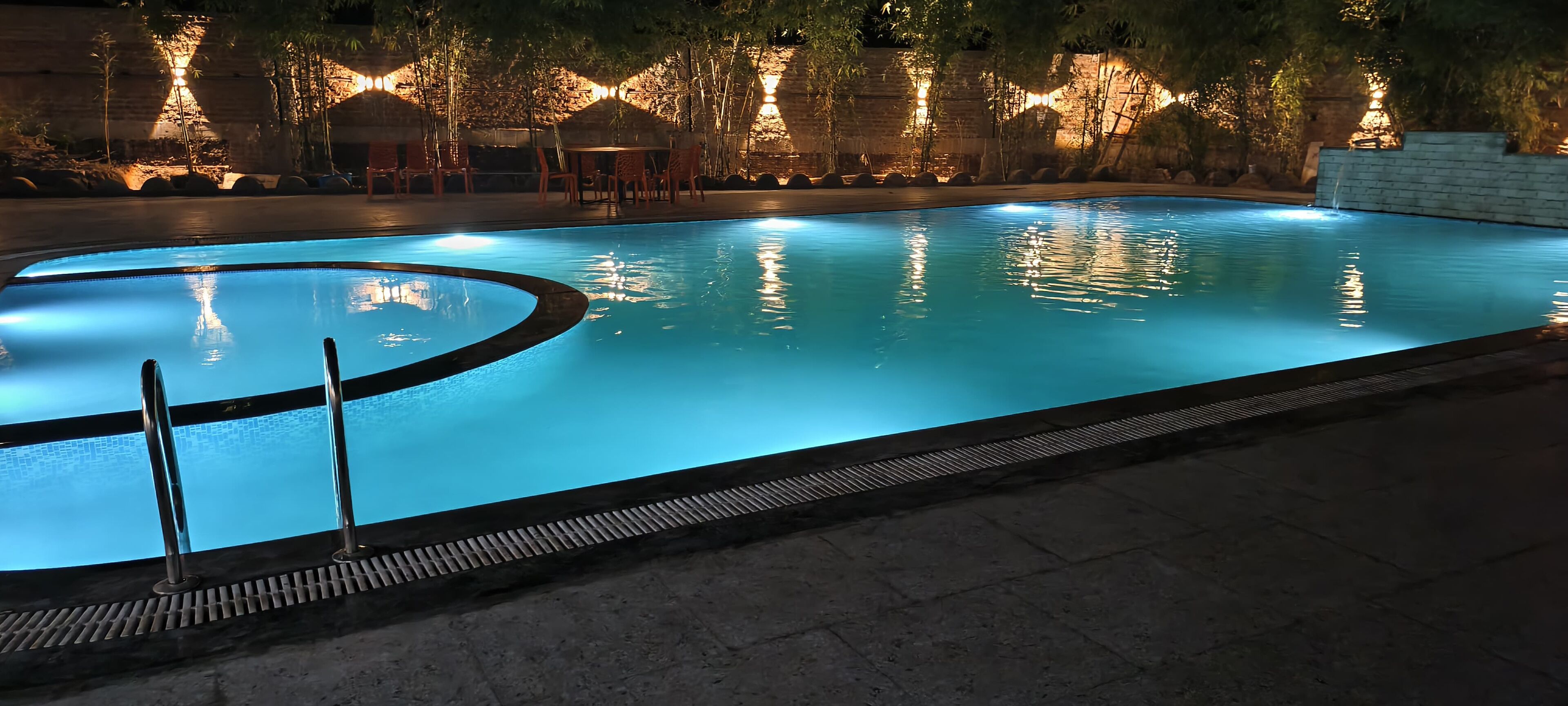 Piscina com borda curva, cercada por um muro de pedra e árvores.