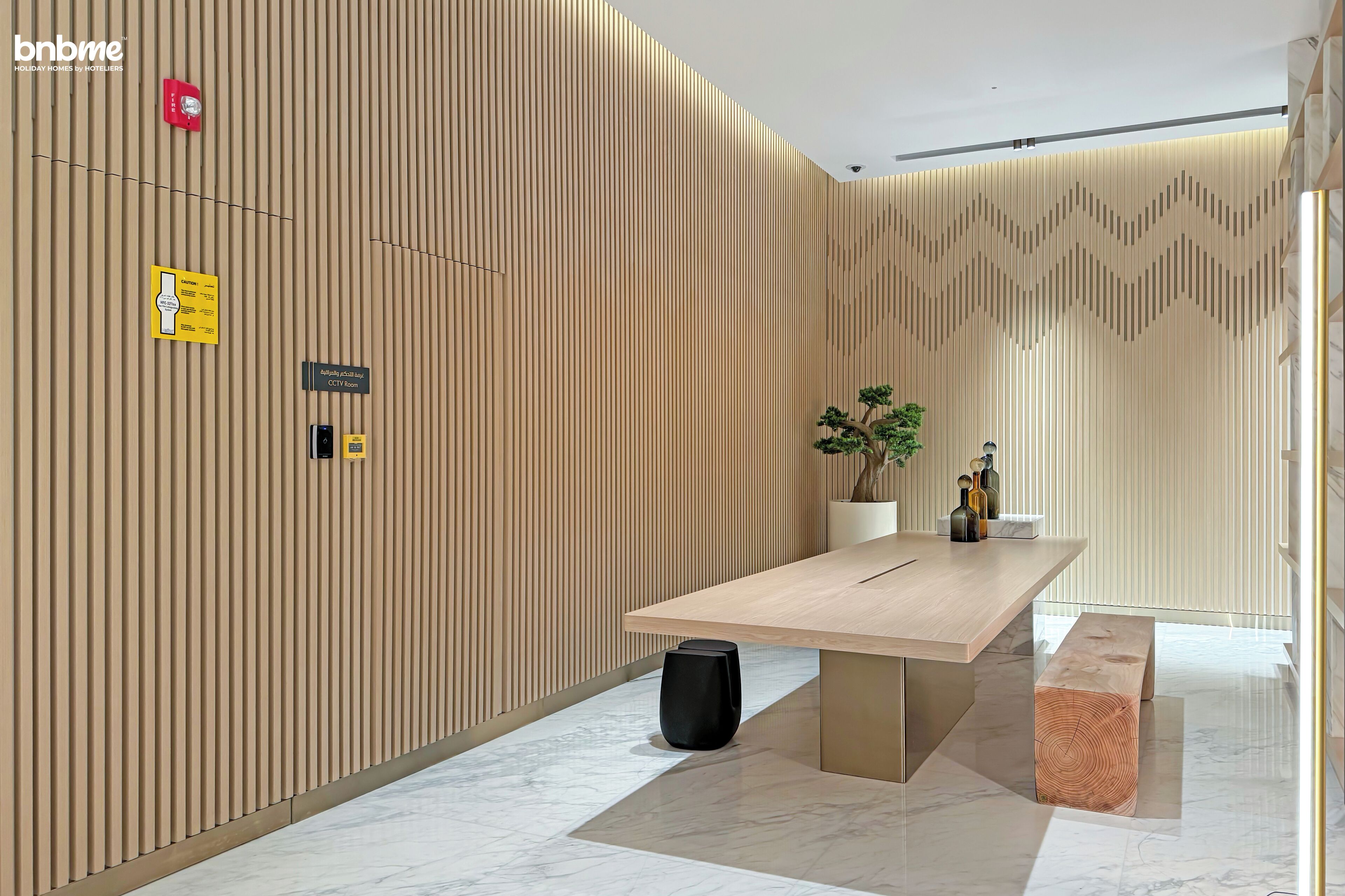 Um hall de hotel moderno com painel de parede de madeira, balcão de recepção, planta em vaso e um banco.