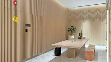 Um hall de hotel moderno com painel de parede de madeira, balcão de recepção, planta em vaso e um banco.