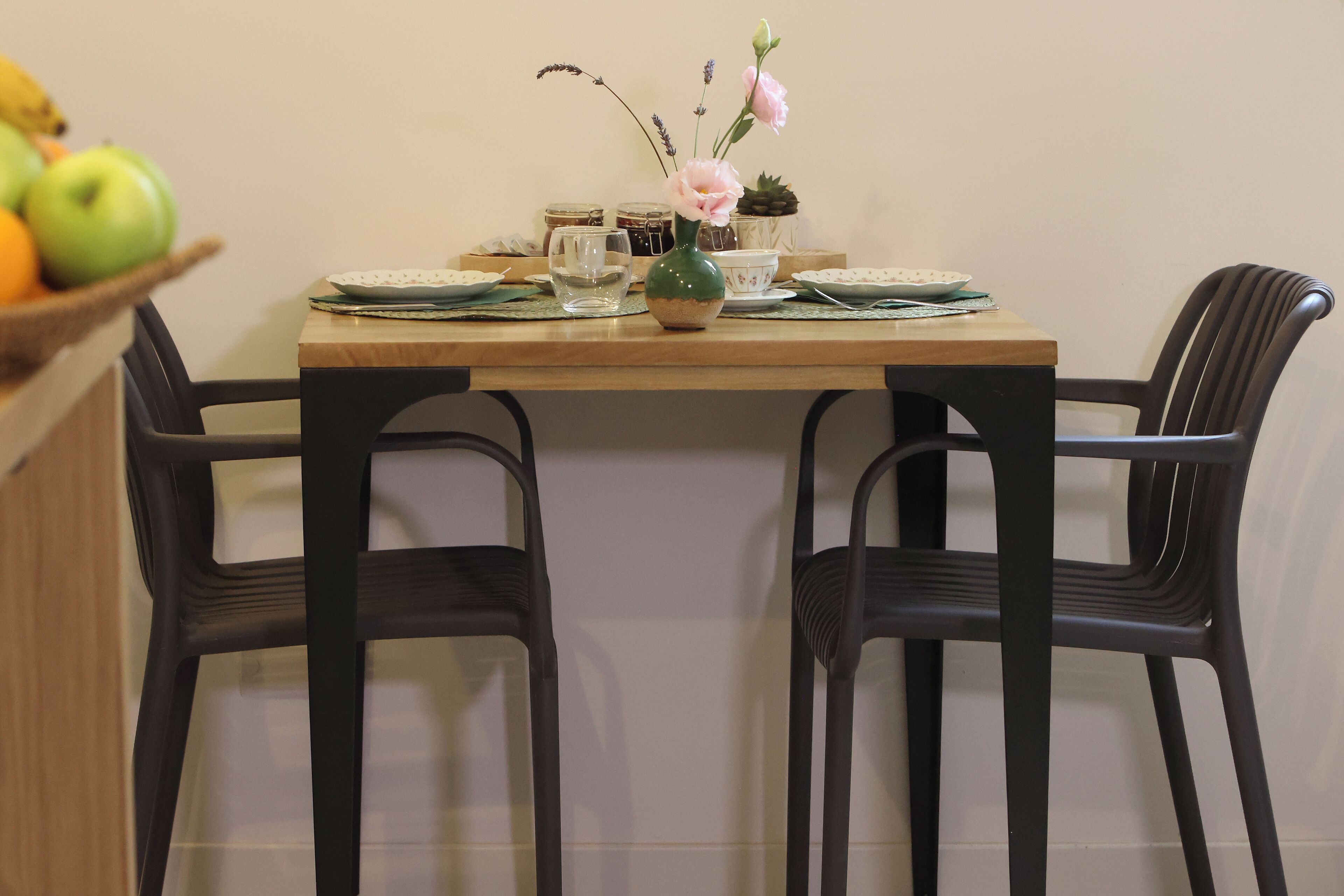 Uma mesa de jantar com um vaso de flores, pratos e uma tigela de frutas.