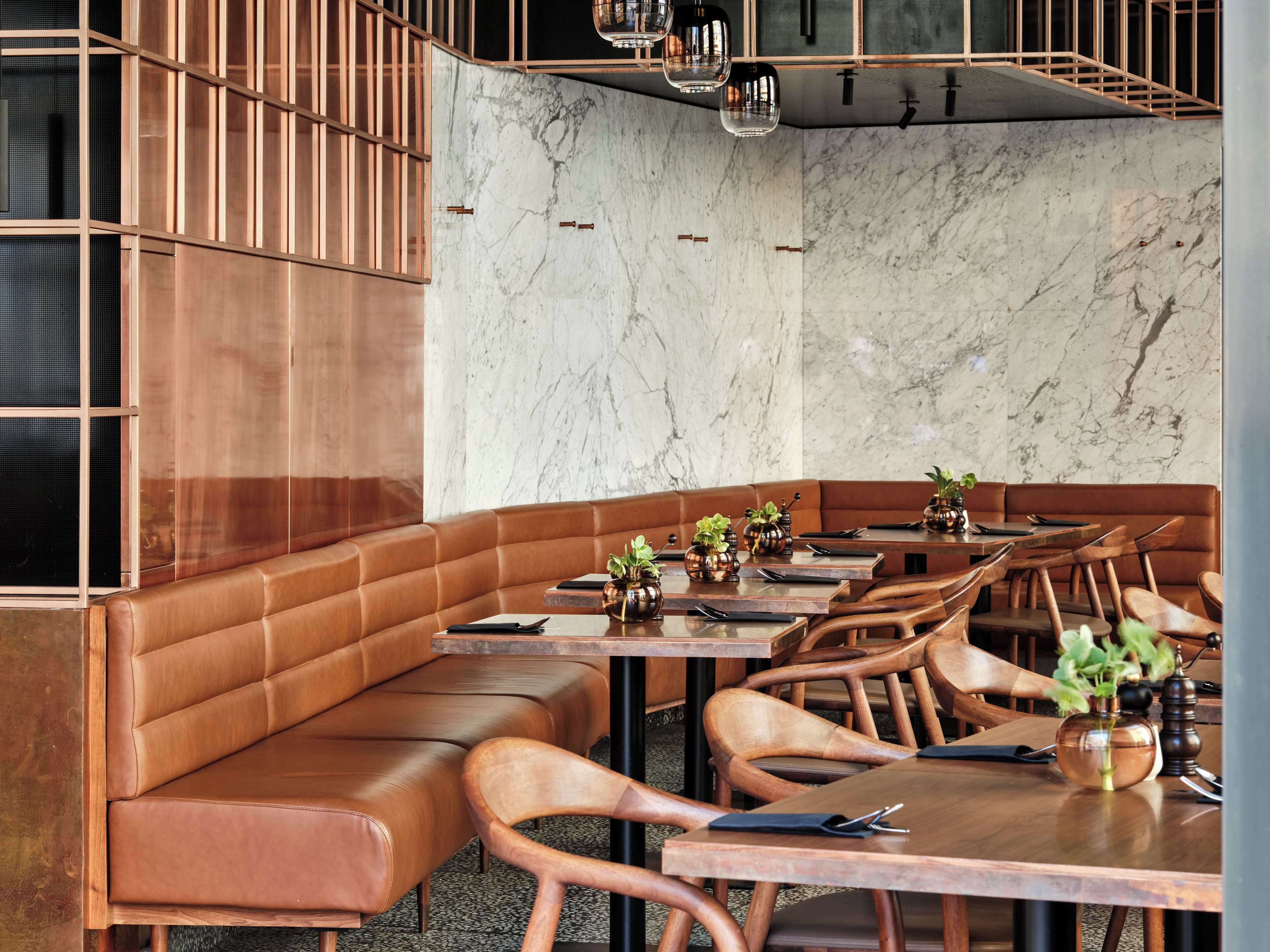 Um interior de restaurante moderno com assentos de couro, mesas de madeira e paredes de mármore.