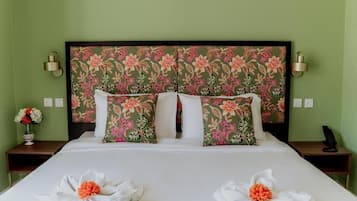 Quarto de hotel com cabeceira floral, duas almofadas, cama com toalhas, mesa de cabeceira com telefone e um vaso com flores.